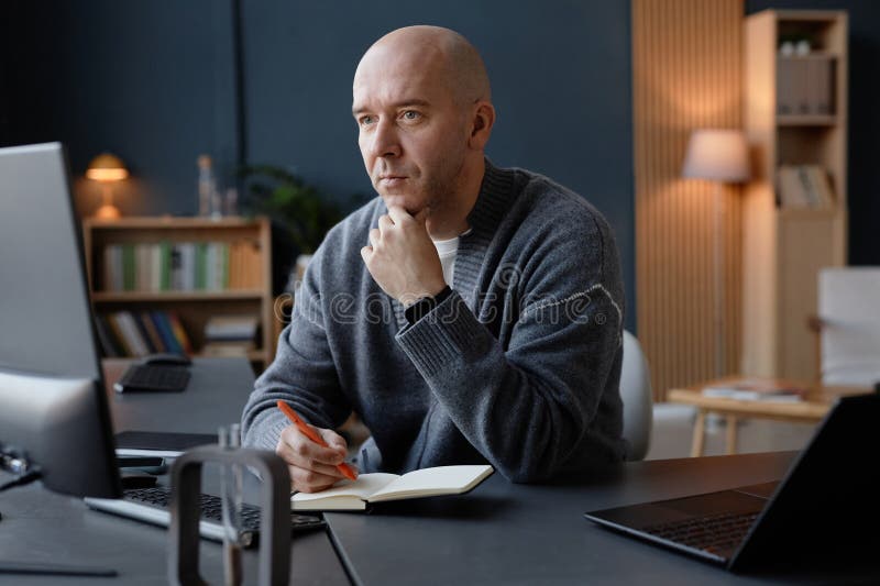 Bald Man Writing in Notebook Using Computer while Thinking Over Task in ...