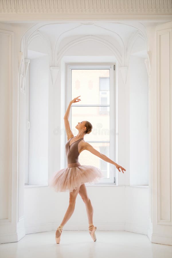 Ballerina in Beige Leotard and Tutu Gracefully Poses on Pointe in a Bright Ballet Studio Stock ...