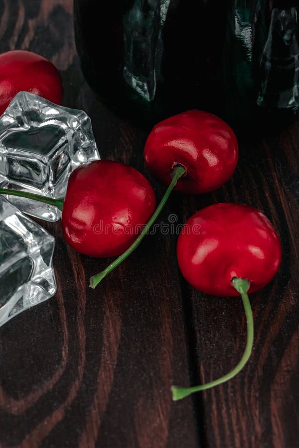 Banch of Red Cherry and Ice Cubes on Black Wet Table. and a Bottle of ...