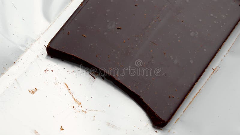 A Bar of Dark Chocolate with Broken Edge on Opened White Paper Wrapper ...
