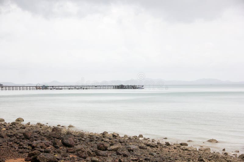 Beach with Rocky Shore and Long Pier Under Overcast Sky Stock Photo ...