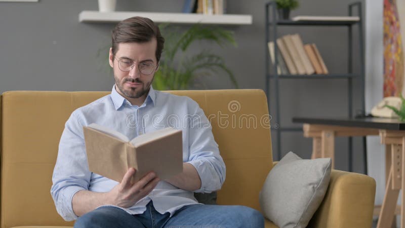 Young Man Thinking while Reading Book on Sofa Stock Photo - Image of ...