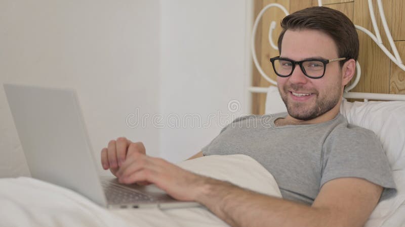 Young Man in Bed Smiling at Camera, Using Laptop Stock Image - Image of ...