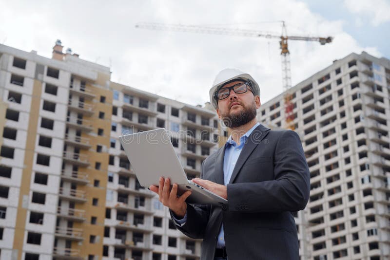 Bearded Building Inspector Making Notes on Laptop at Construction Site ...