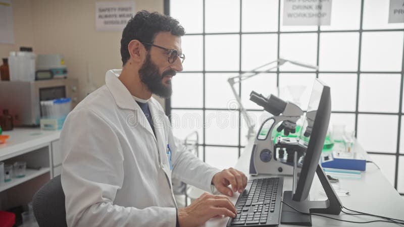 A Bearded Man in a Lab Coat Studies a Computer Screen in a Laboratory ...