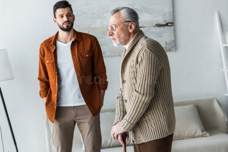 Bearded Son Standing with Hands in Pockets and Looking at Sad Senior ...