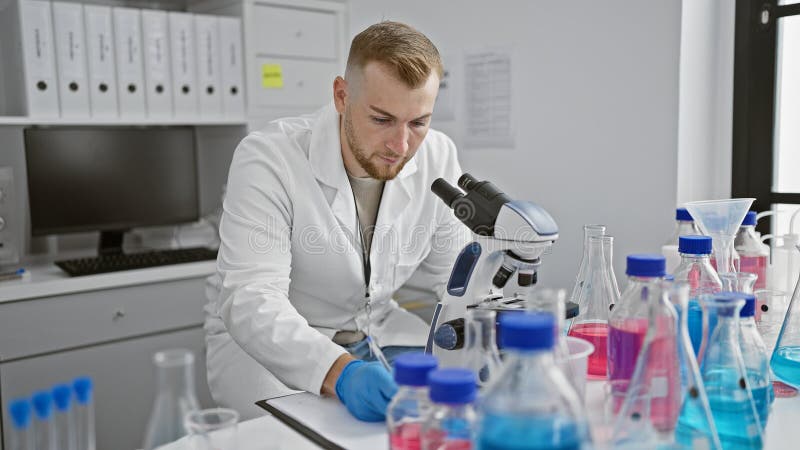 Bearded Young Man in Lab Coat Analyzing Samples with Microscope in ...