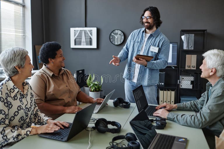 Bearded Young Man Leading Computer Class for Seniors Using Laptops at ...