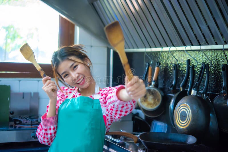 Beautiful Asian Home Cook Wearing an Apron is Holding a Spatula with ... Beautiful Asian Home Cook Wearing an Apron is Holding a Spatula with ...