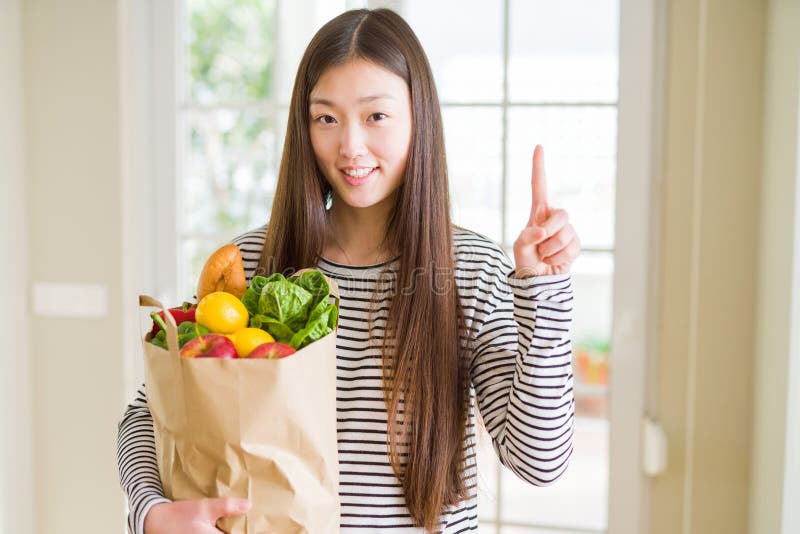 Beautiful Asian Woman Holding Paper Bag Of Fresh Groceries Surprised