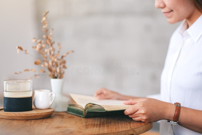 A Beautiful Asian Woman Holding And Reading A Book While Sitting In