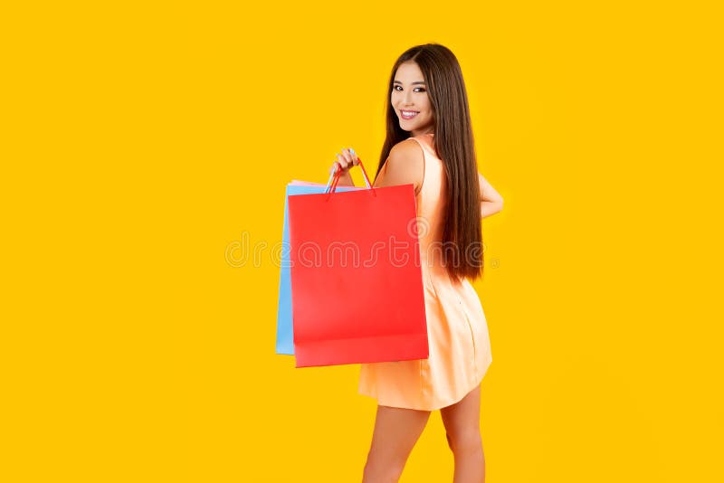 Beautiful Asian Woman Holding Shopping Bags On A Yellow Background