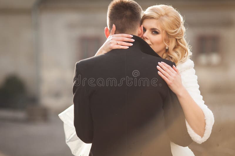 Beautiful Blonde Bride Kissing Handsome Groom In Black Coat In T Stock