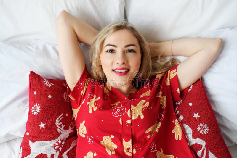 Beautiful Blonde Girl In Red Pajamas Lies On The Bed Smiles And Looks At The Camera Stock Image