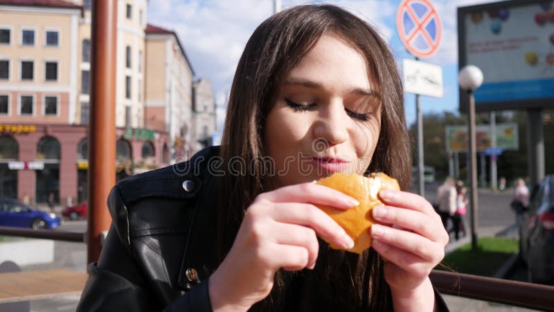 Beautiful Brunette Girl Eats A Cheeseburger Or Hamburger In A Street