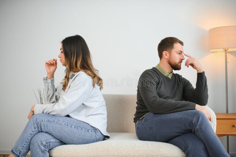 Beautiful Couple Is Sitting Back To Back On The Couch While Having A