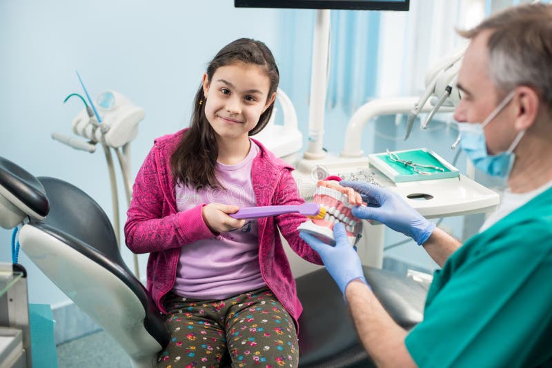 Girl In Dentist Chair Educating Proper Tooth Brushing By Her Pediatric