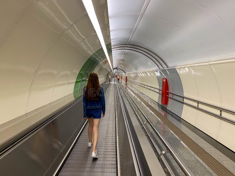 A Beautiful Girl Walks Along The Travolator In The Subway Tunnel To Go To Another Underground