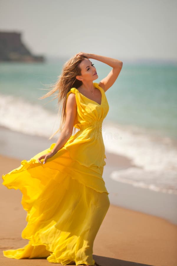 Young Beautiful Girl Walks Op The Sandy Beach In A Flying Yellow Dress