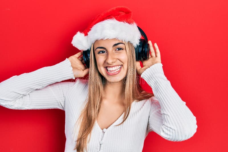 Beautiful Hispanic Woman Wearing Christmas Hat And Headphones Smiling
