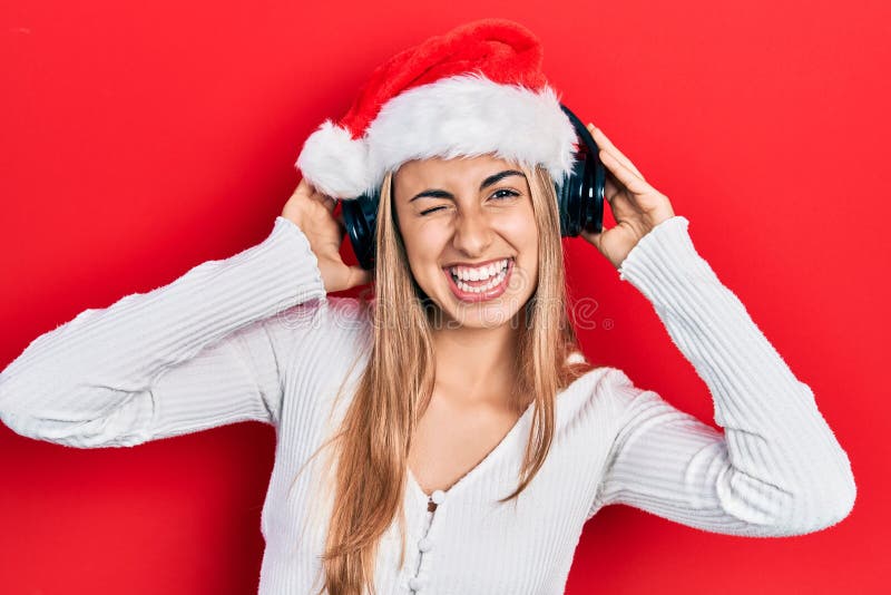 Beautiful Hispanic Woman Wearing Christmas Hat And Headphones Winking