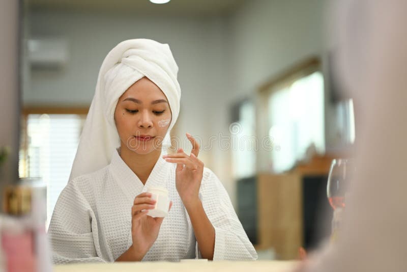 Beautiful Millennial Woman In Bathrobe Applying Facial Skincare Cream