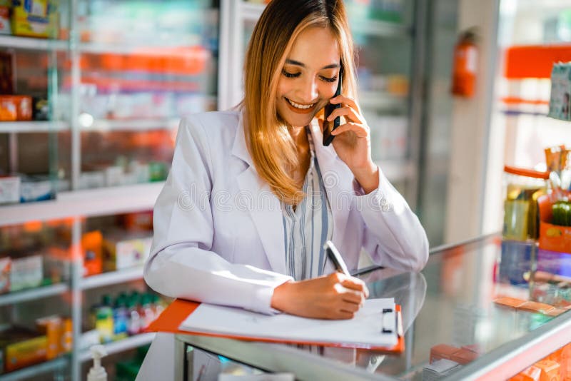 Beautiful Pharmacist Making a Call while Writing Request on Paper Stock ...