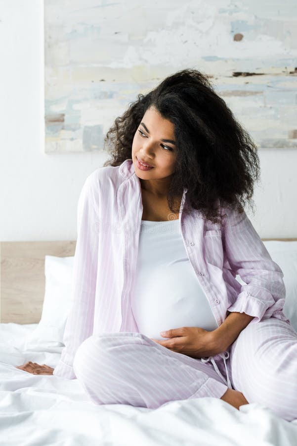 Pregnant African American Woman Touching Belly While Standing On Grey