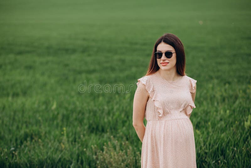 Beautiful Pregnant Woman Wearing A Dress And Hat In A Green Field With