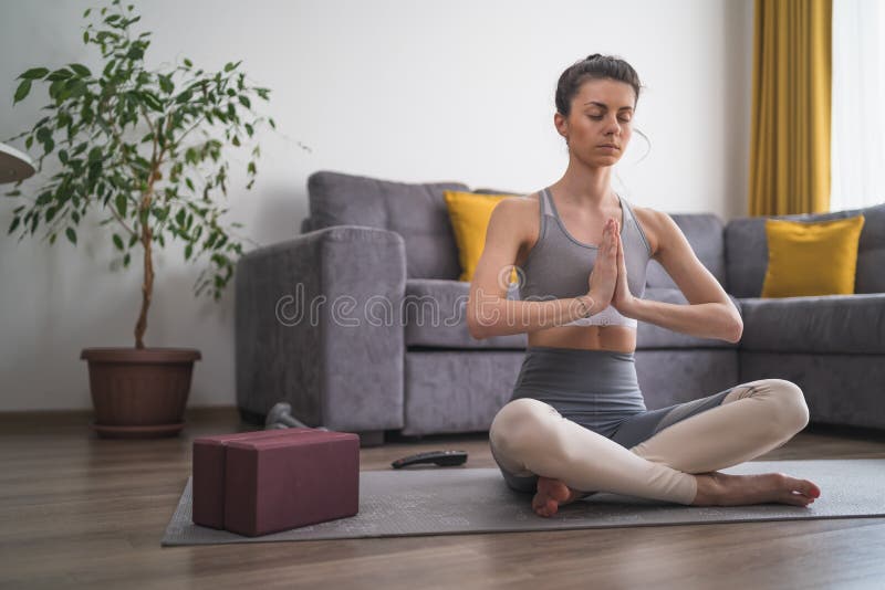 Beautiful Woman In Namaste Yoga Pose Sitting On Yoga Mat At Home Stock