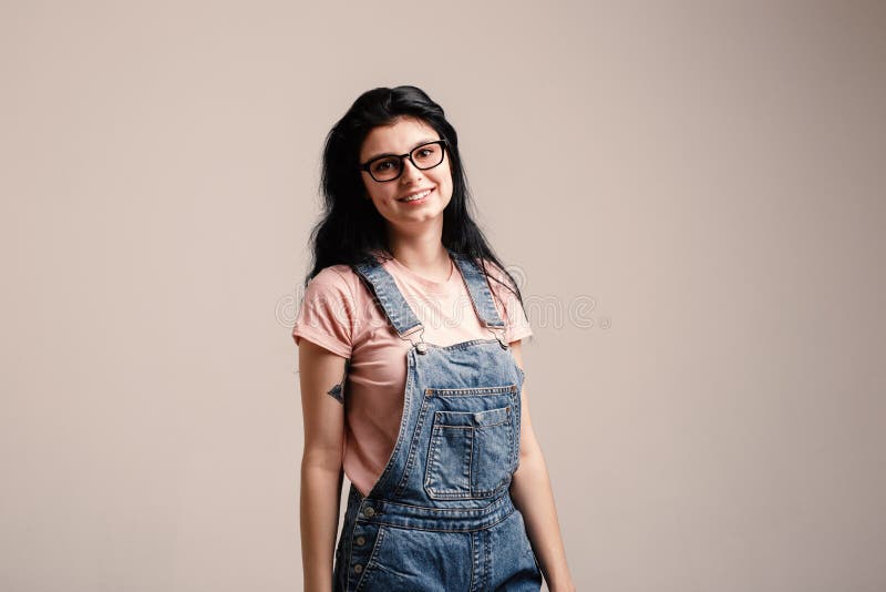 Beautiful Smiling Brunette Girl Wearing Glasses In Denim Overall Posing