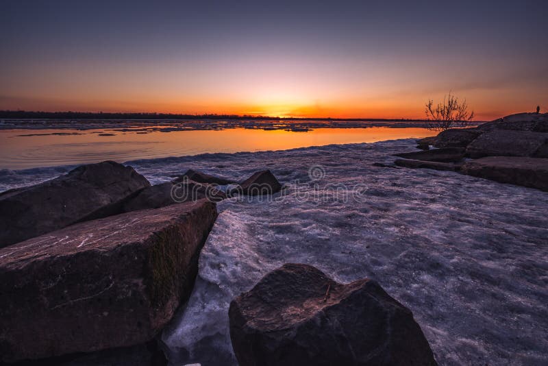 A Beautiful Sunset Over a Large River with Floating Ice and Rocks on ...
