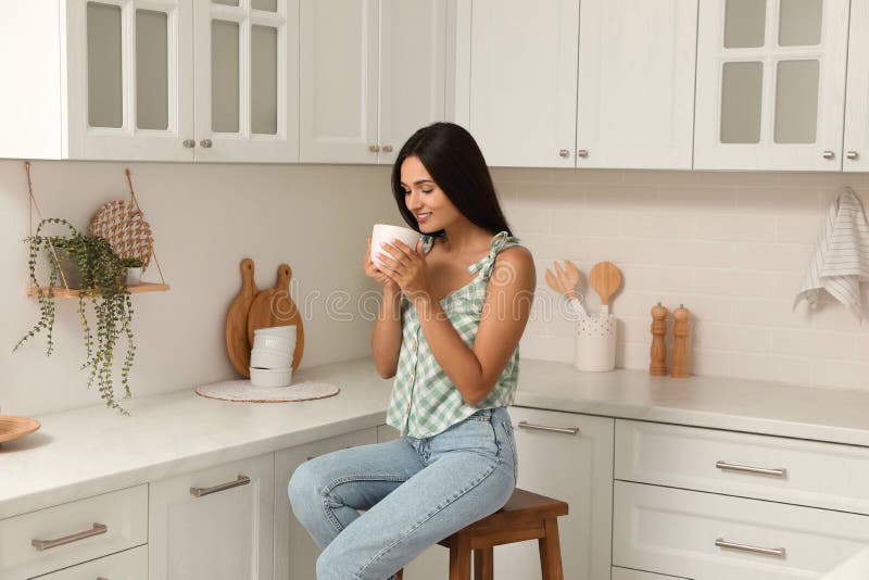 Beautiful Young Woman with Cup of Tea Sitting on Stool in Kitchen Stock ...