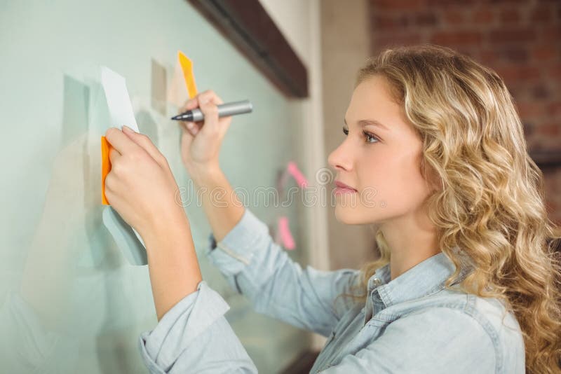 Beautiful Woman Holding Sticky Note while Writing on Glass Board Stock ...