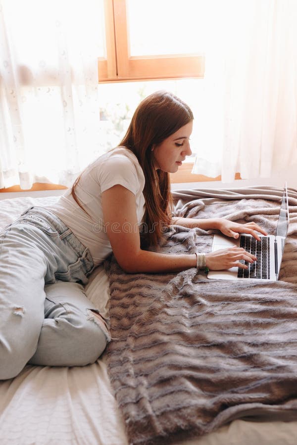 Beautiful Woman Lying In Her Cozy Bed Writing On Her Laptop Stock Image