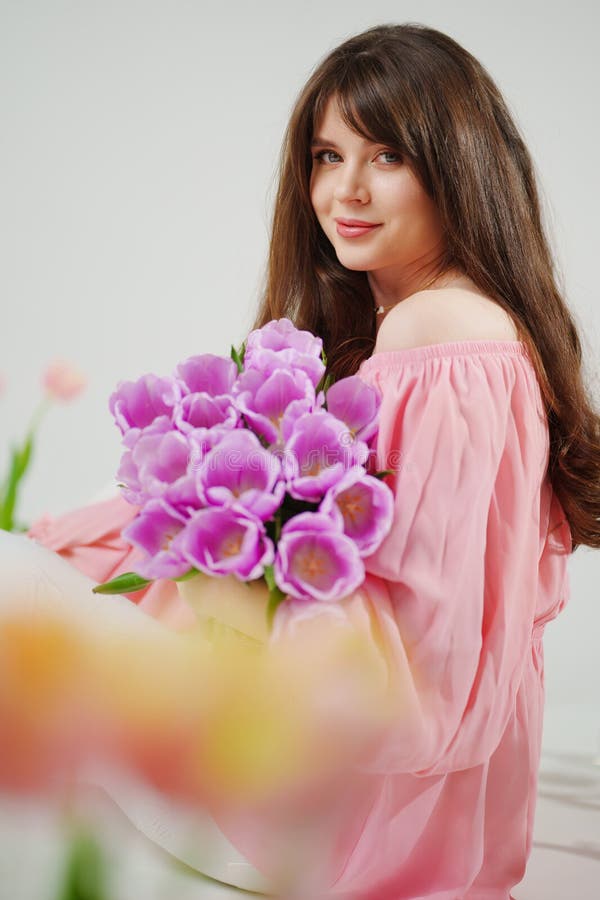 Beautiful Young Brunette Woman With Long Hair In Pink With A Bouquet Of