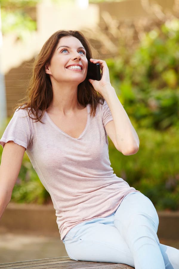 Beautiful Young Lady Sitting Outdoors and Talking on Cell Phone Stock ...