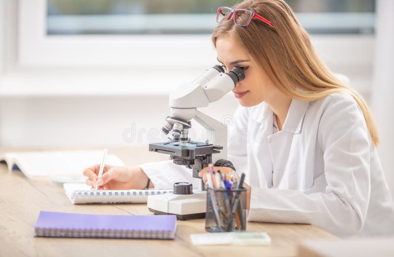 Beautiful Young Researcher Looking into a Microscope, Writing Down ...