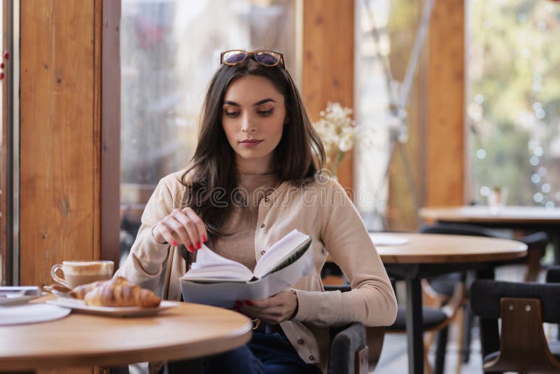 Beautiful Young Woman Reading A Book While Sitting At The Cafe Stock