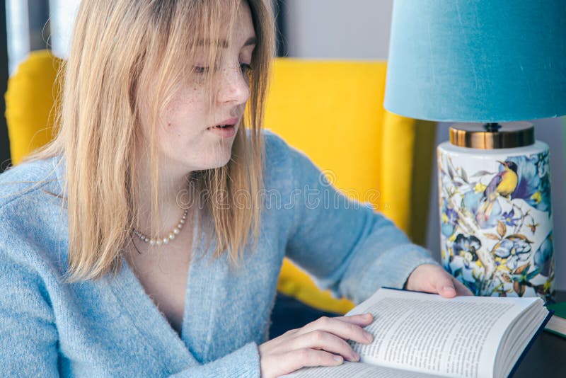 Beautiful Young Woman Is Reading A Book While Sitting At The Table