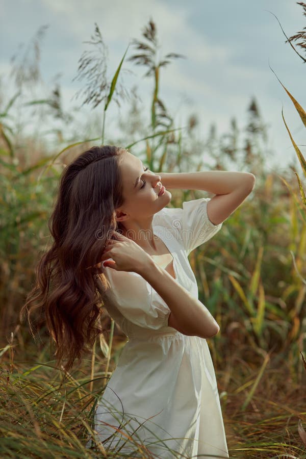 Beautiful Young Woman In White Summer Dress Is Sitting In Tall Grass In