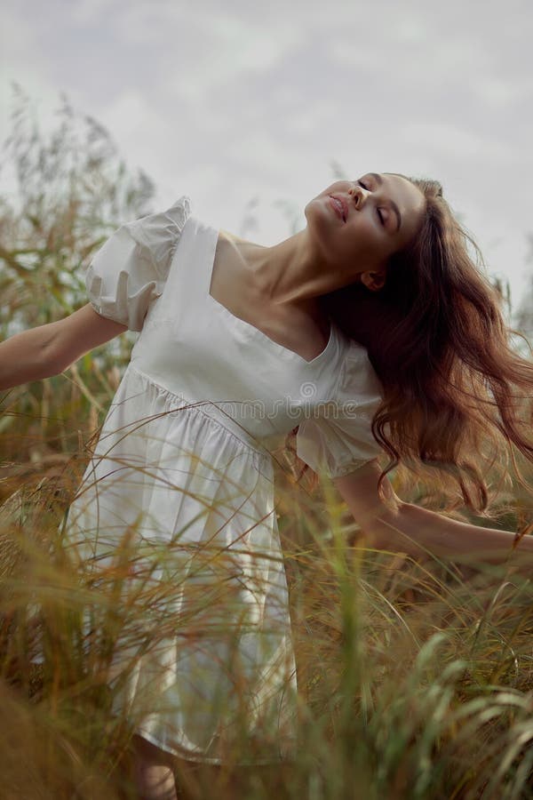 Beautiful Young Woman In White Summer Dress Is Sitting In Tall Grass In