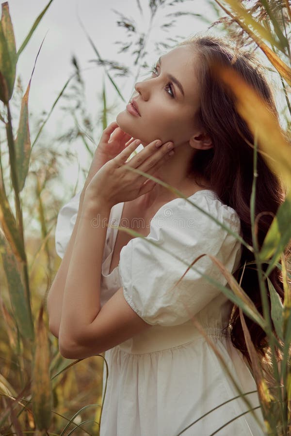 Beautiful Young Woman In White Summer Dress Is Sitting In Tall Grass In