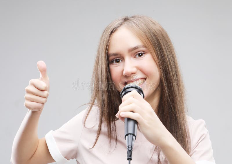 Beauty Model Girl Singer with a Microphone Over Light Grey Background ...