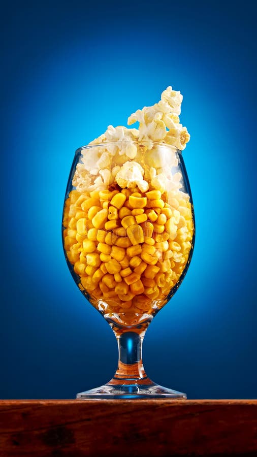 Beer Glass Filled with Corn Kernels and Pop Corn Stands on Table Against Blue Studio Background ...