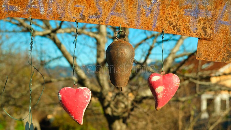 A Bell Hangs from a Metal Bar with Three Red Hearts Hanging from it ...
