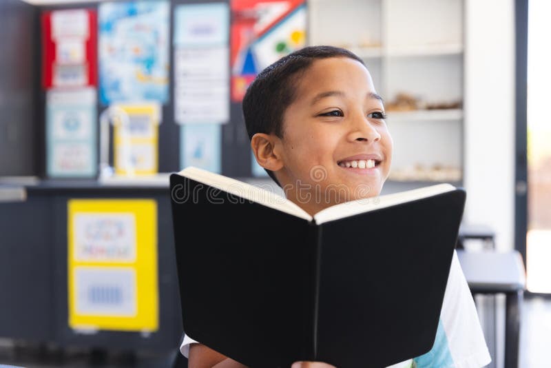 Biracial Boy Enjoys Reading a Book in the Classroom at School Stock ...