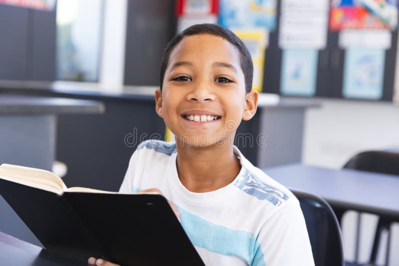 Biracial Boy Reading a Book in the Classroom at School Stock Photo ...