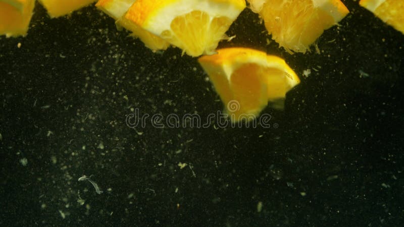 On a Black Background, Many Pieces of Orange Fall into the Liquid ...