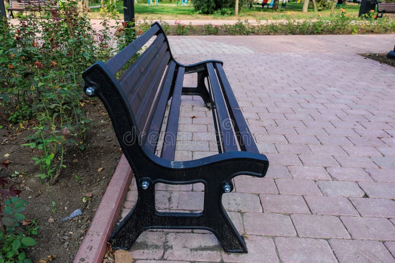 A Black Bench Sits on a Brick Walkway in a Park, Broken Element Stock ...